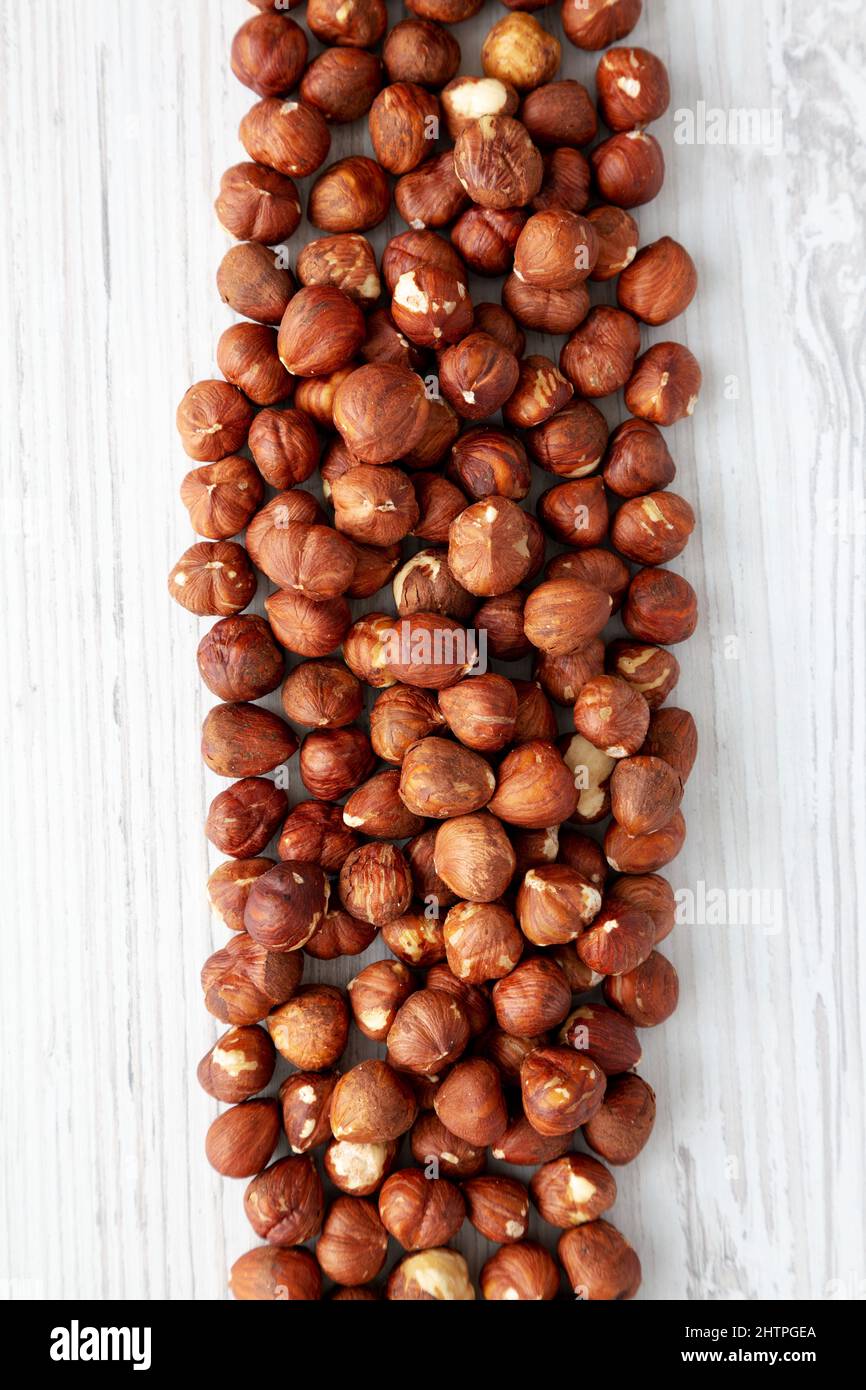 Unshelled Hazelnut in a Bowl on a white wooden surface, top view. Flat ...