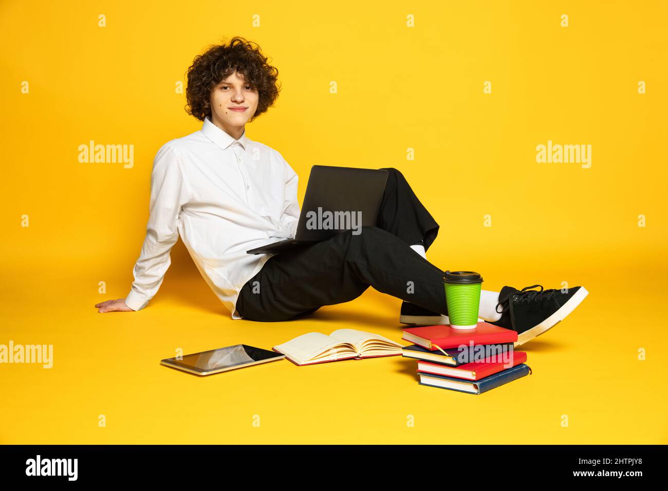 Portrait of young boy, student sitting on floor and studying isolated ...