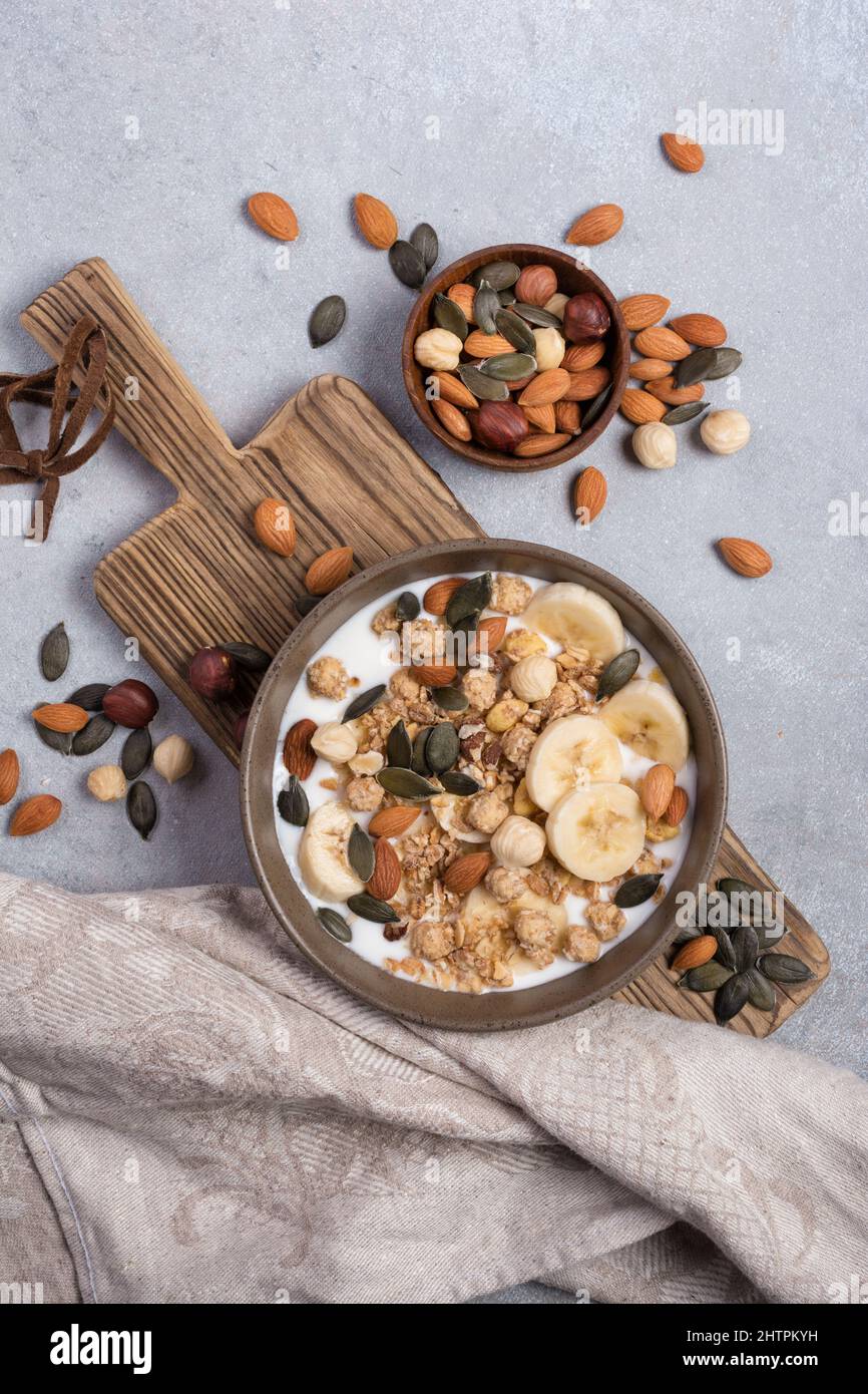 Top view of granola with yogurt, fresh banana, almonds and hazelnuts, pumpkin seeds for healthy ...
