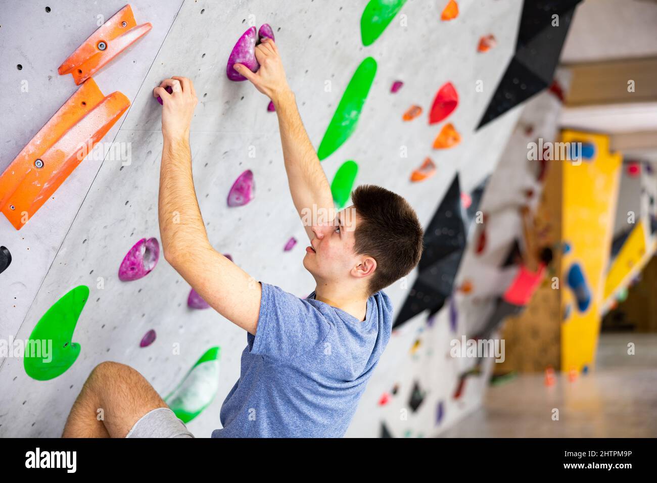 Young man grabbing ledges of artificial climbing wall Stock Photo - Alamy