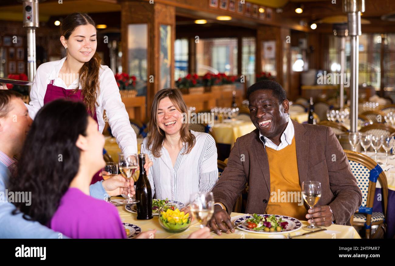 Young waitress serving cheerful people during dinner in restaurant ...