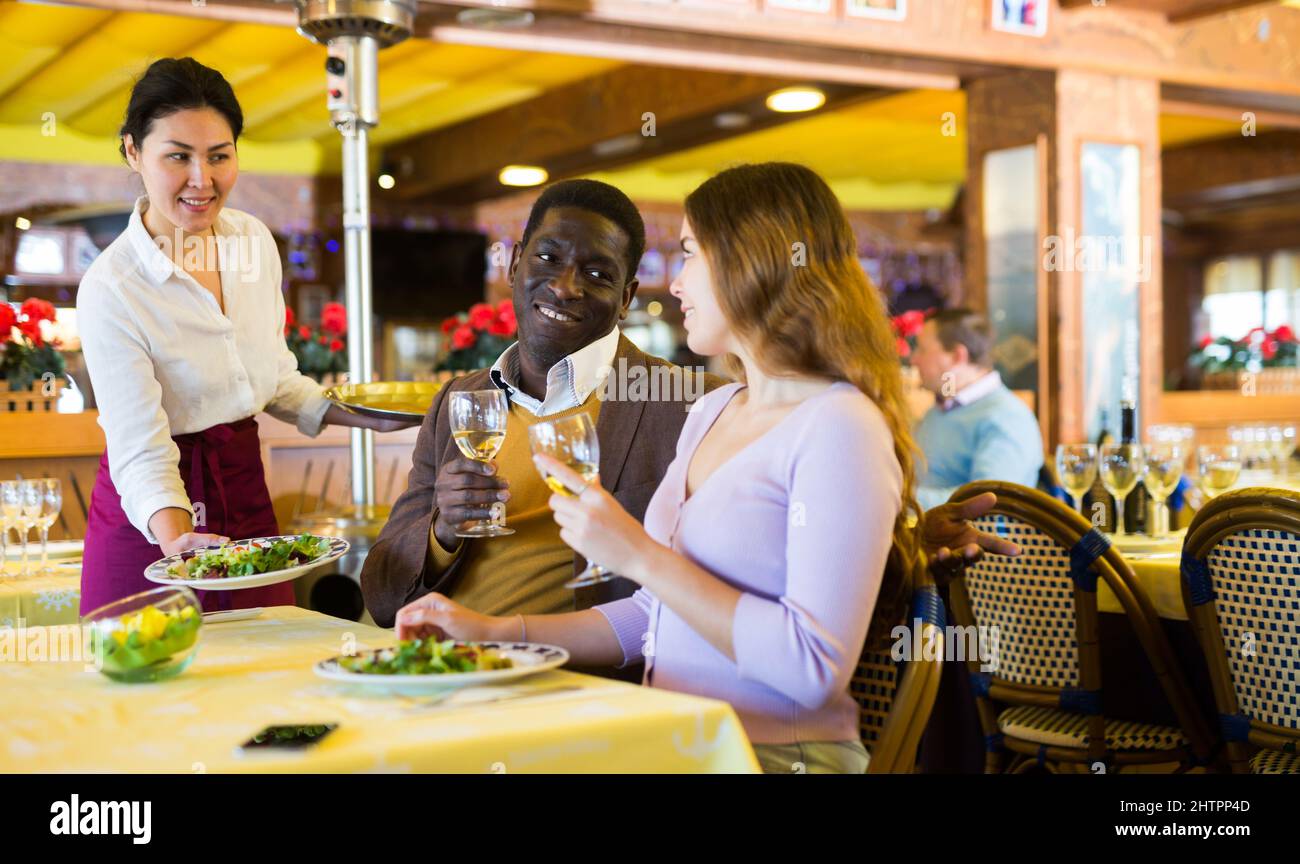 Polite Asian waitress serving dishes to biracial couple in restaurant ...