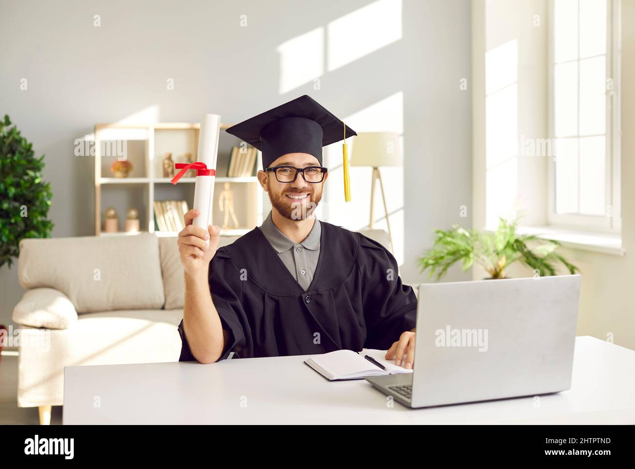 Happy student who got his online degree sitting at desk, holding ...
