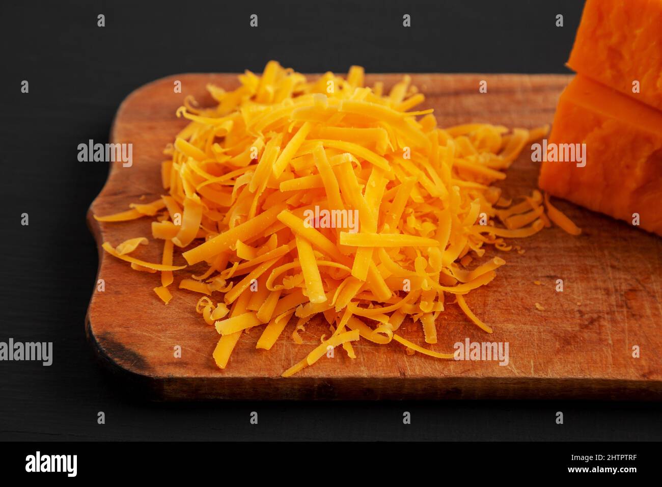 Shredded Sharp Cheddar Cheese on a rustic wooden board on a black ...