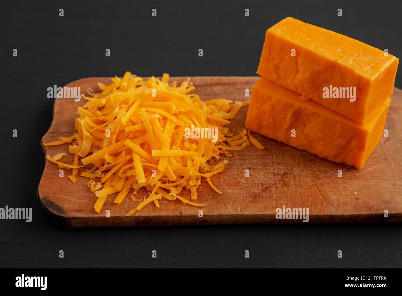 Shredded Sharp Cheddar Cheese on a rustic wooden board on a black ...