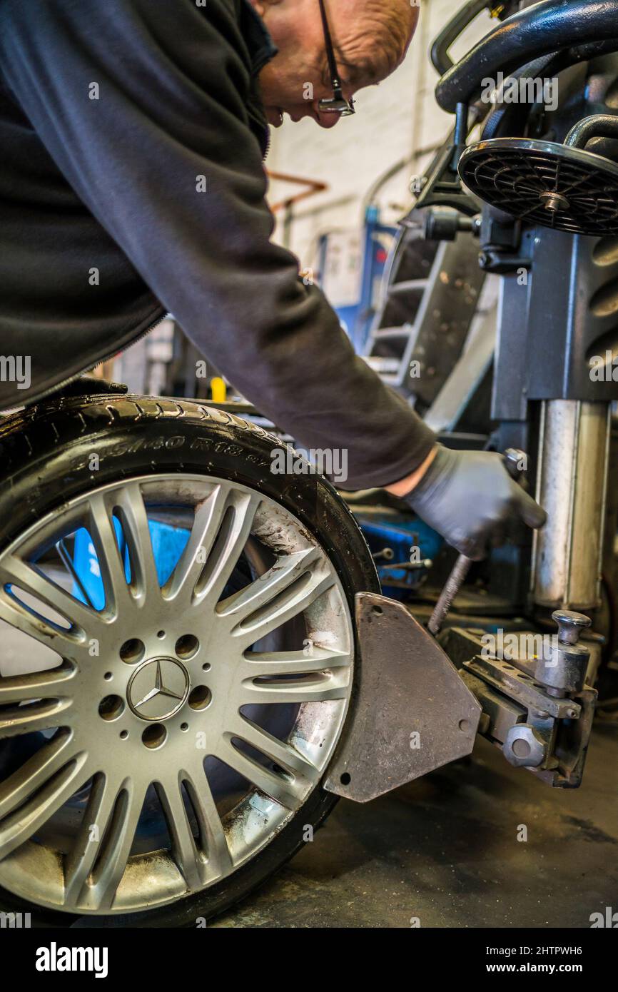 Tyre garage workshop. Garage staff fremove a tyre on an alloy wheel ...