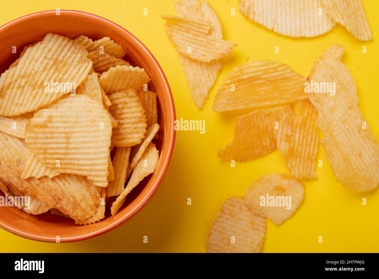Overhead close-up of potato chips in bowl and on yellow background ...