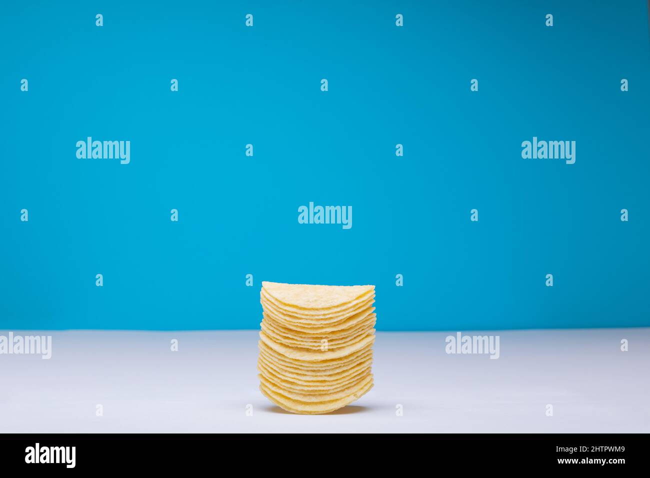 Stack of potato chips on table against blue background with copy space ...