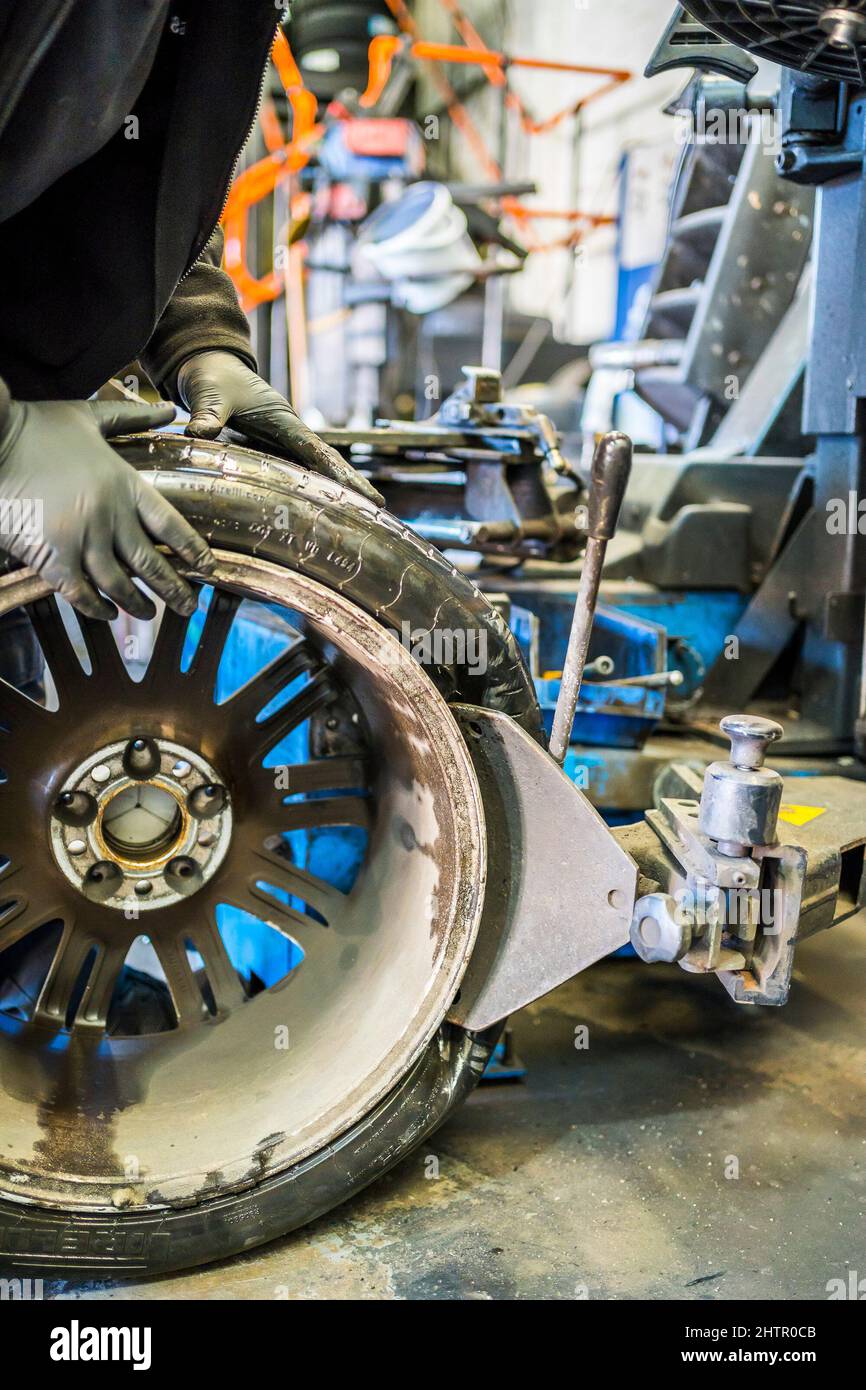 UK tyre garage workshop. Garage staff remove a tyre on an alloy wheel ...