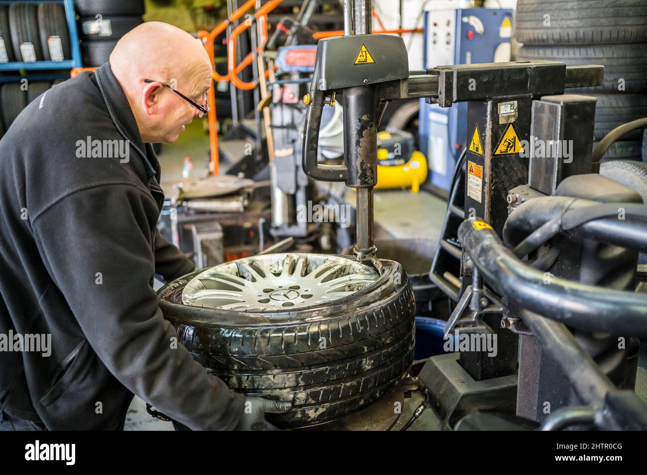 UK tyre garage workshop. Garage staff removes a tyre on an alloy wheel ...
