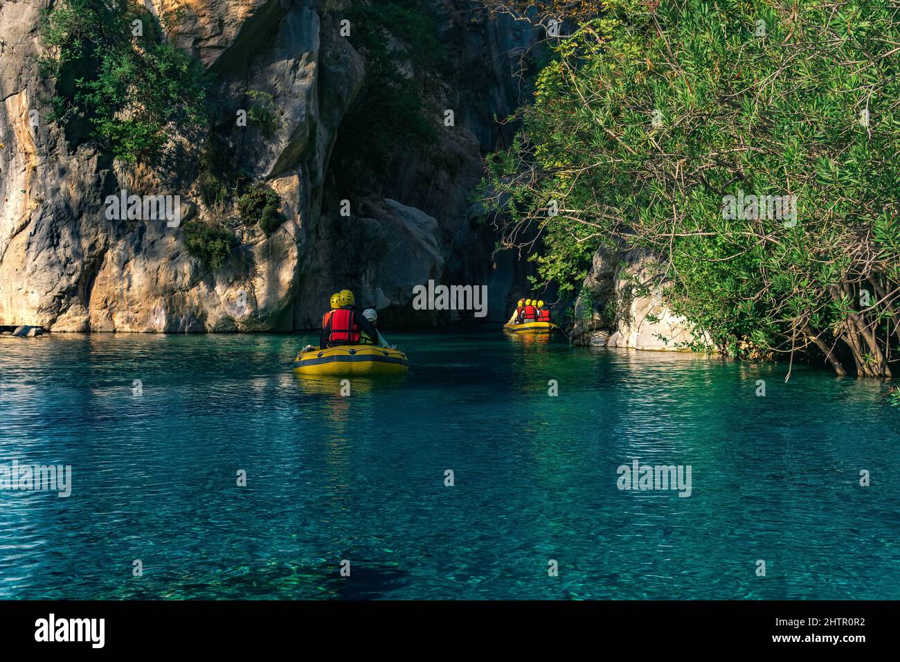 tourists on an inflatable boats float down a rocky canyon with blue ...