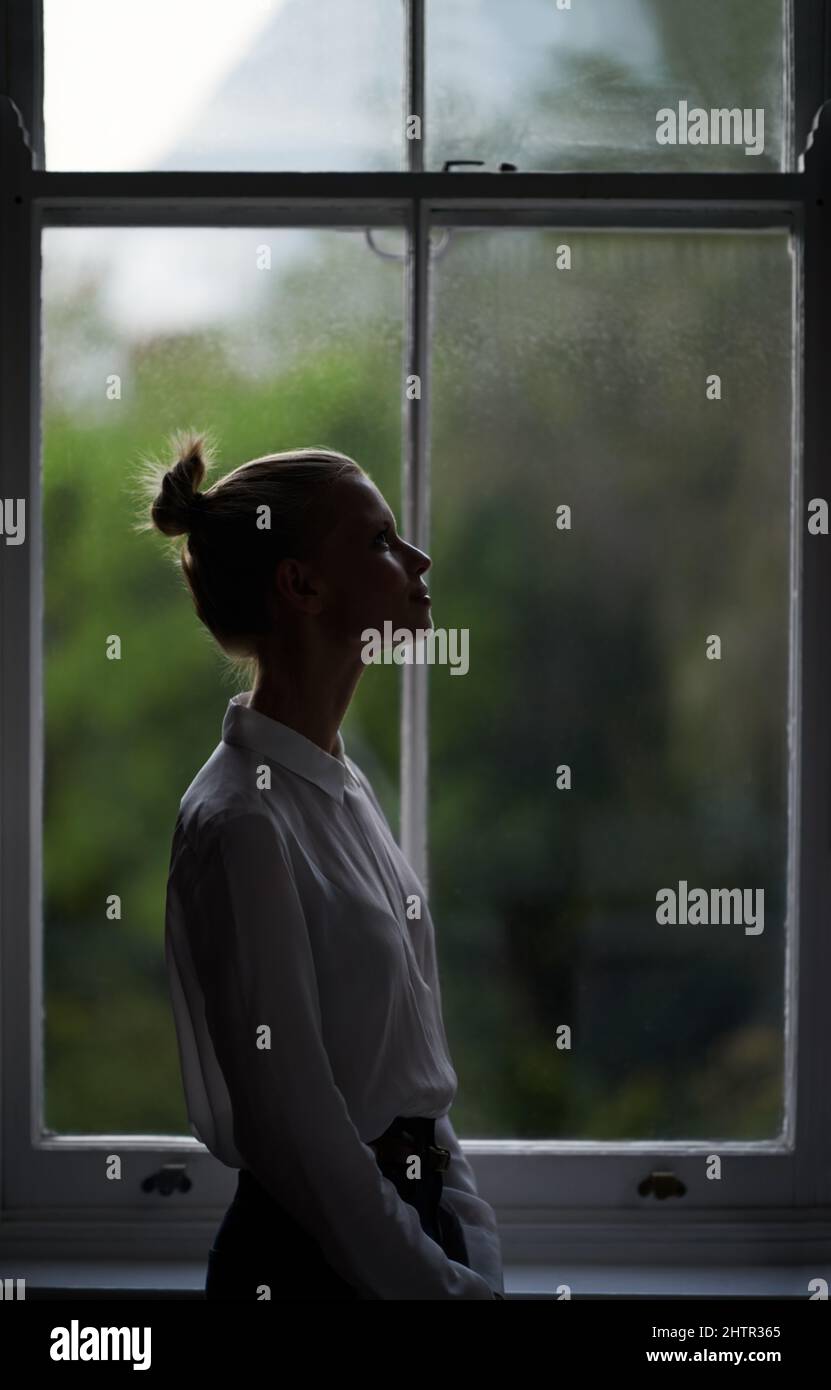 Reflection by the window. A beautiful young woman standing by a window ...