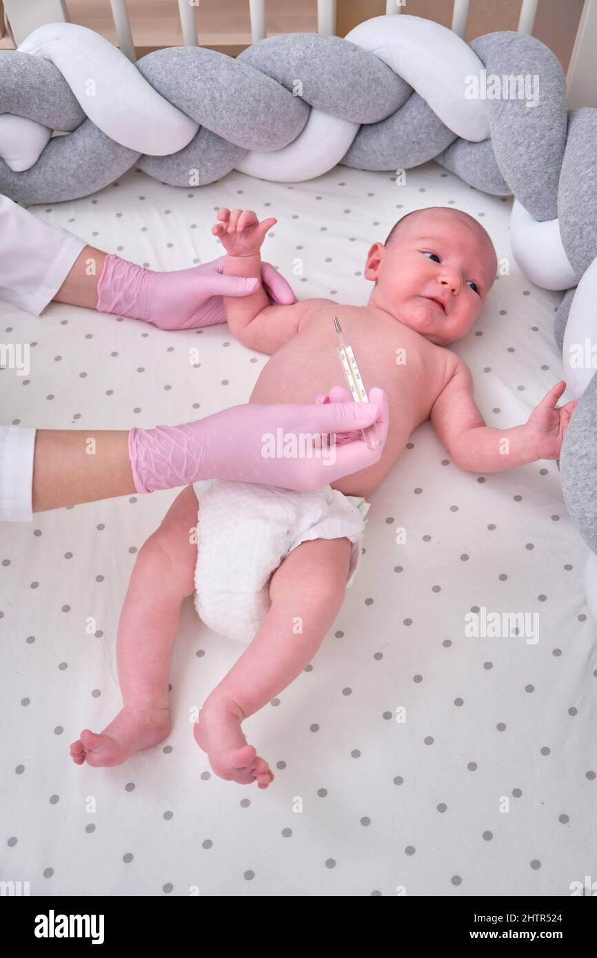 Doctor checks the temperature of the newborn baby with a thermometer. A ...