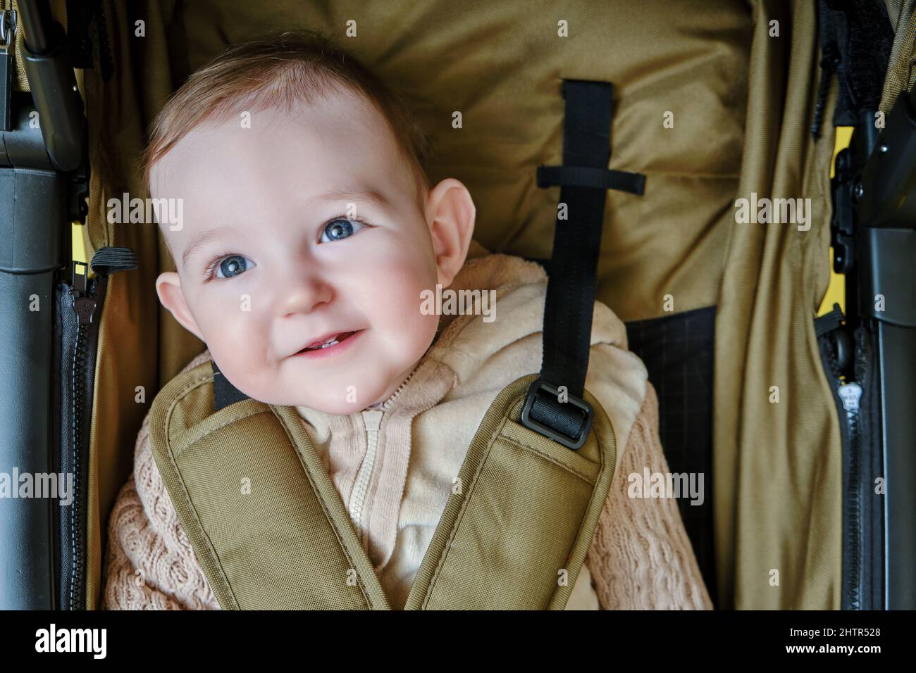 A happy child is sitting in a baby carriage on a studio yellow ...