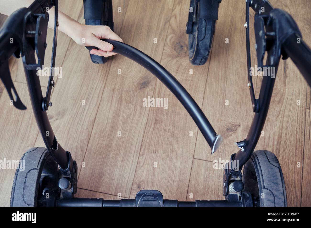 A woman hand holds a broken baby carriage chassis. Damage to the ...