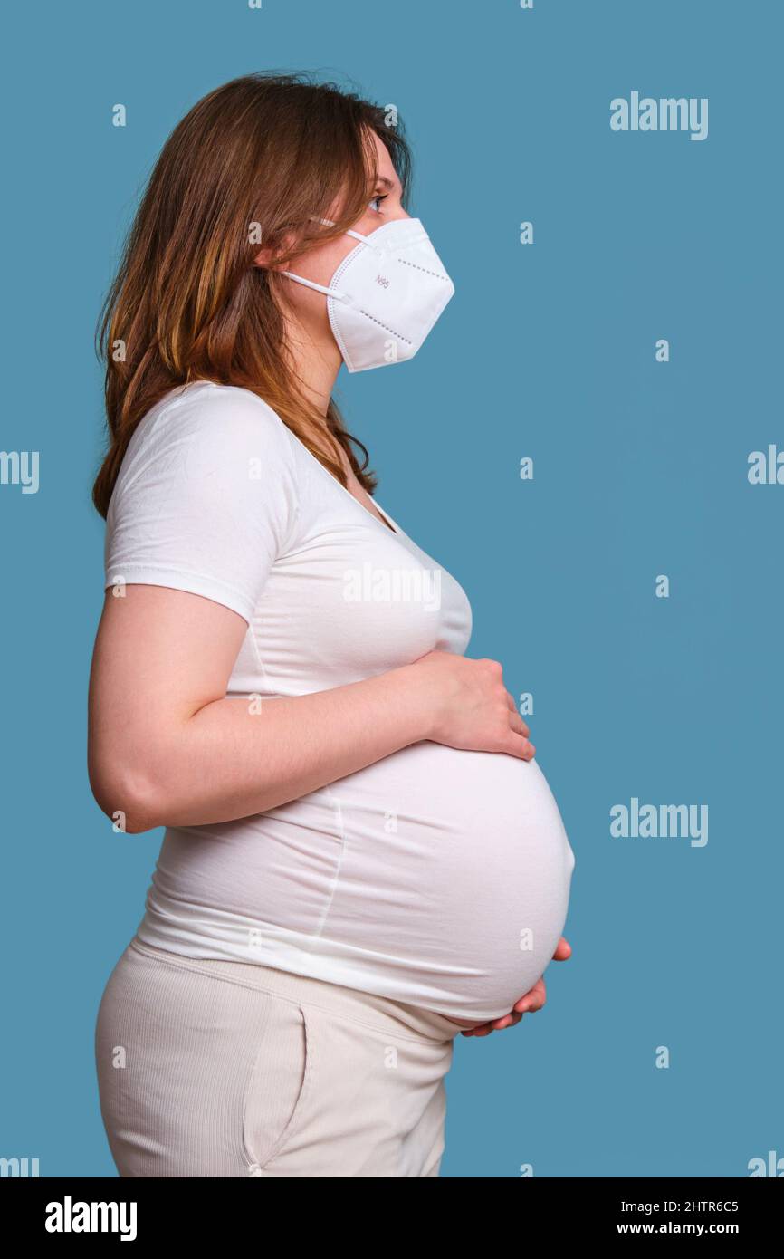 Portrait of a pregnant woman in a medical face mask, blue background ...