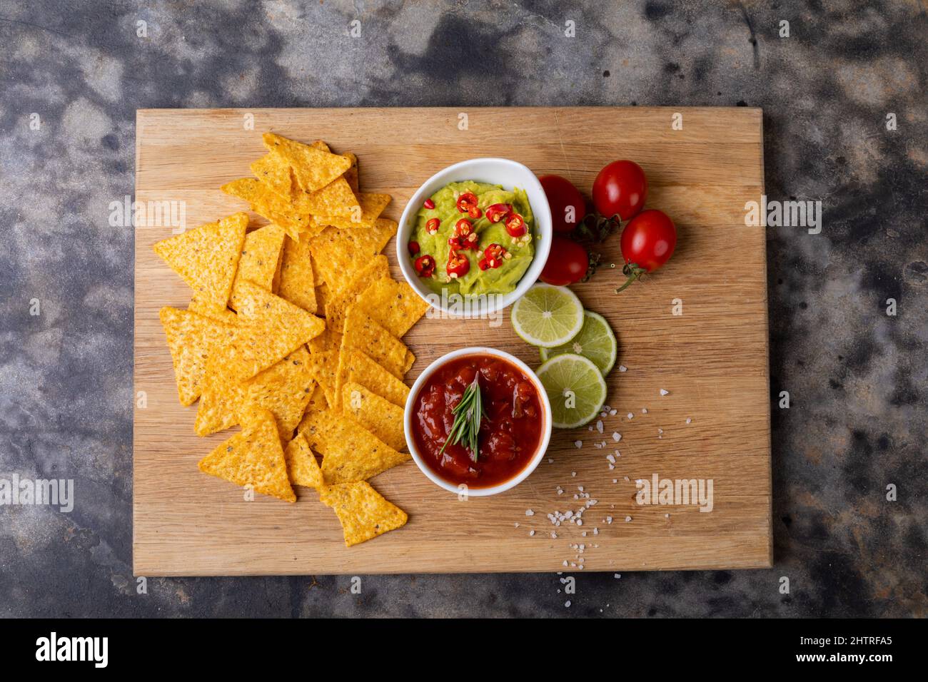 Overhead view of nacho chips with dipping sauces, tomatoes and limes ...