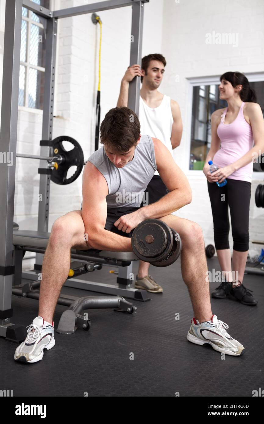 Staying focused. young bodybuilder lifting a weight while two people ...