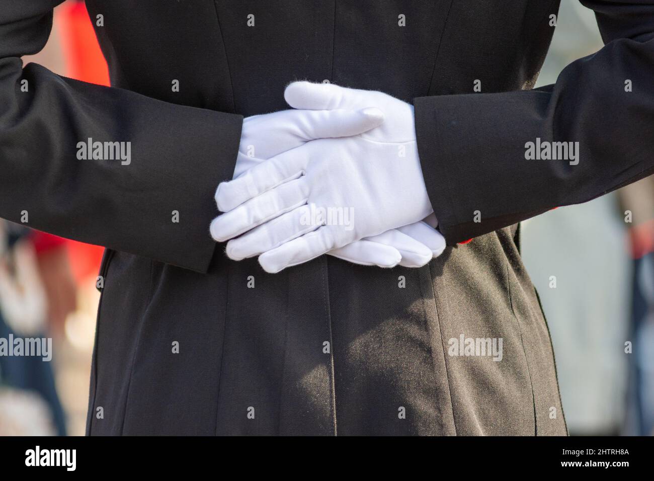 Rear view of a man in a solid suit and gloves holding his hands behind ...