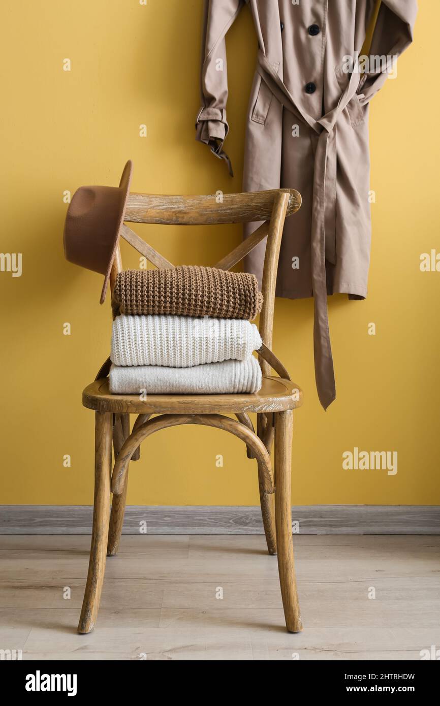 Wooden chair with sweaters, hat and trenchcoat hanging on yellow ...