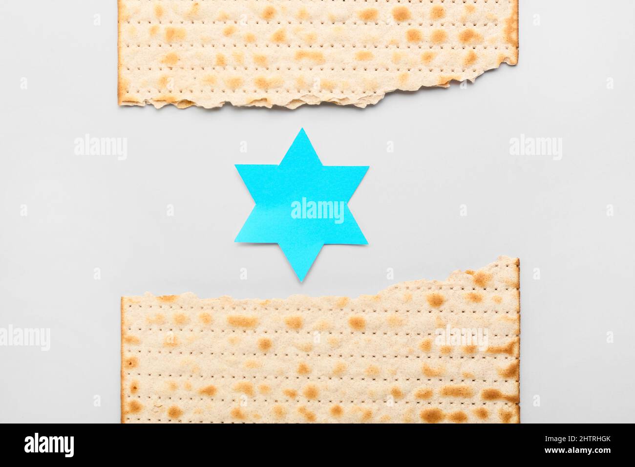 Torn Jewish flatbread matza for Passover with paper David star on light ...