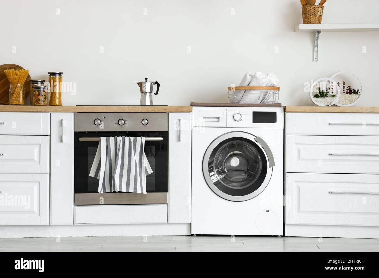Interior of light kitchen with washing machine, oven and white counters ...