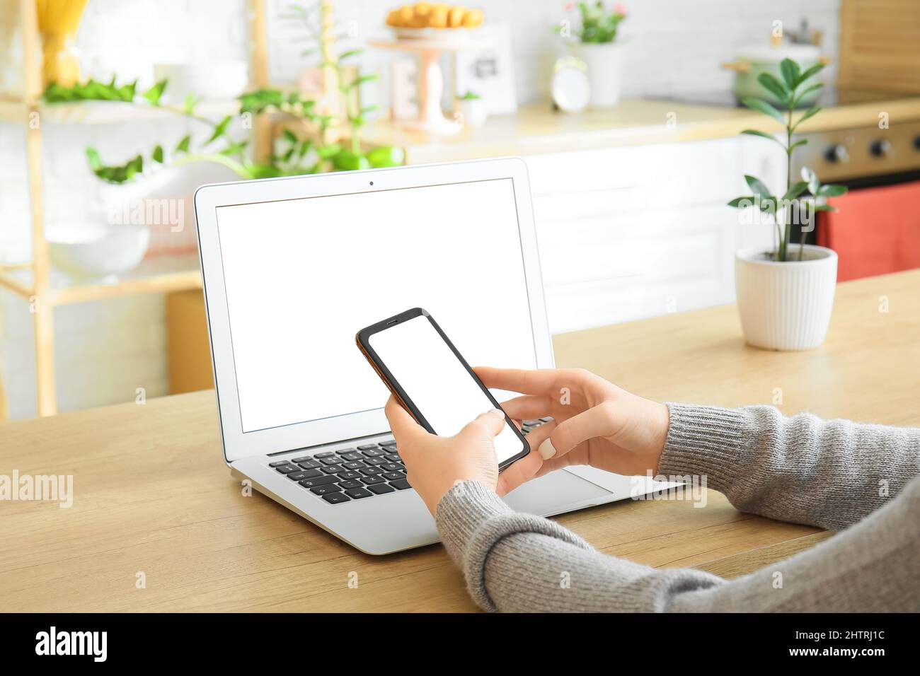 Woman using modern mobile phone on wooden table with laptop in light ...