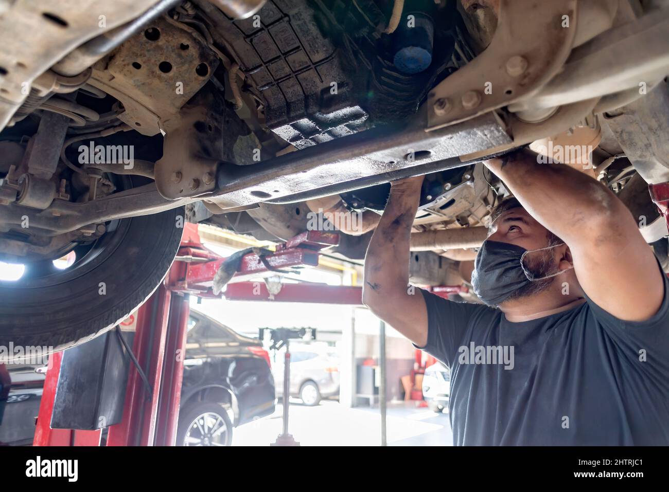 Latin male mechanic working beneath a malfunctioning dirty automobile ...