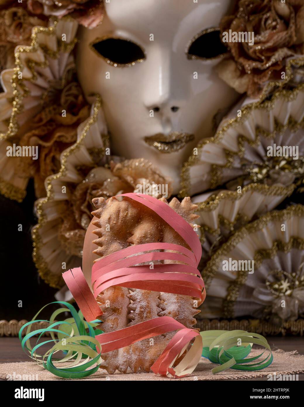 A typical Italian carnival dessert wrapped in streamers with a mask in ...