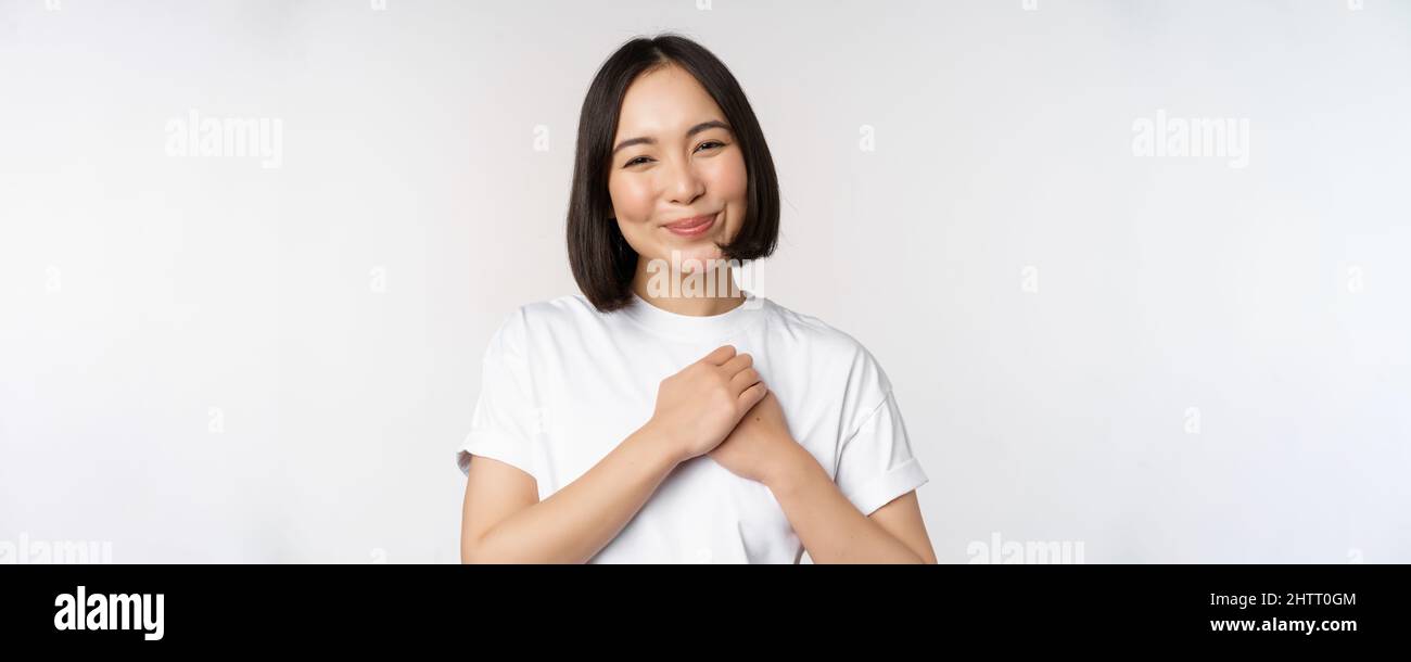 Portrait of carig young asian woman holding hands on heart, gazing with ...