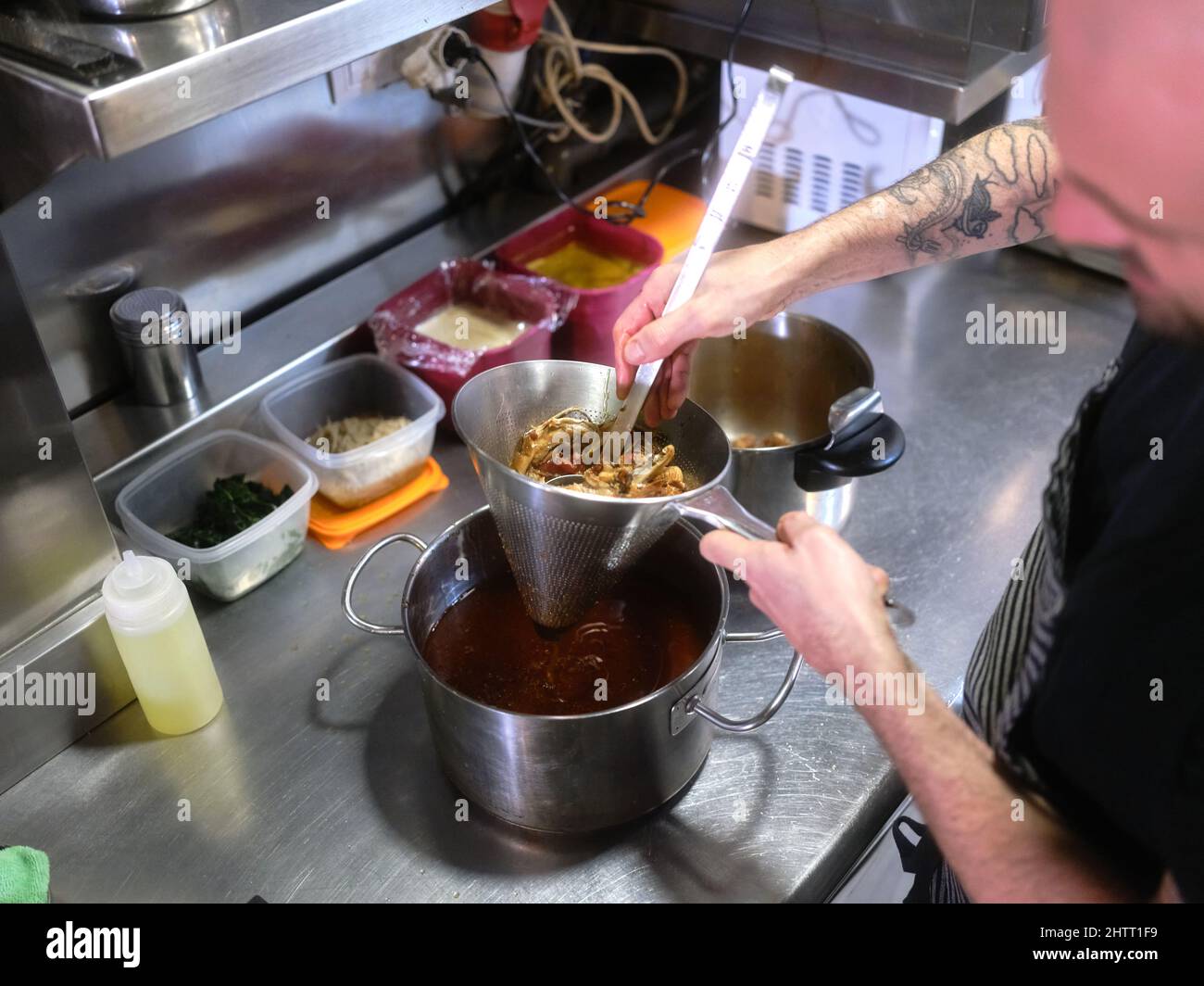 Cook strains food into a pot to prepare a tasting menu in a restaurant ...