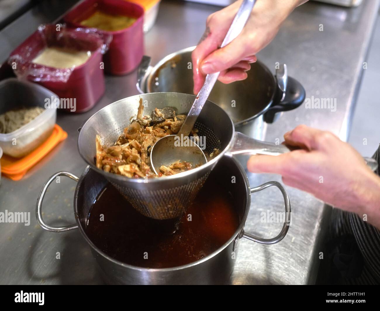 Cook squeezing juice out of food using a strainer in a restaurant ...
