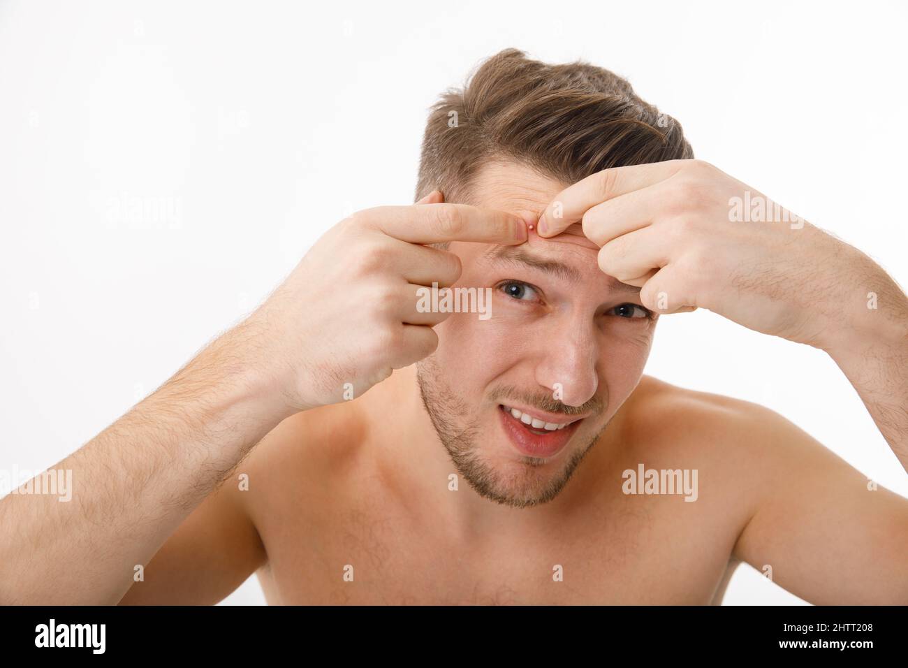 A young man squeezes out a pimple on his face while looking in the ...
