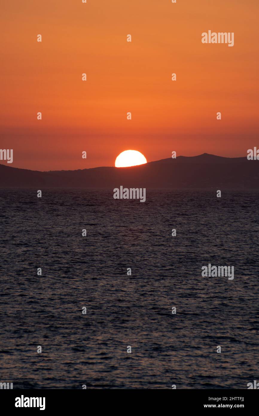 Vertical shot of the sun setting behind the hills at the sea Stock ...