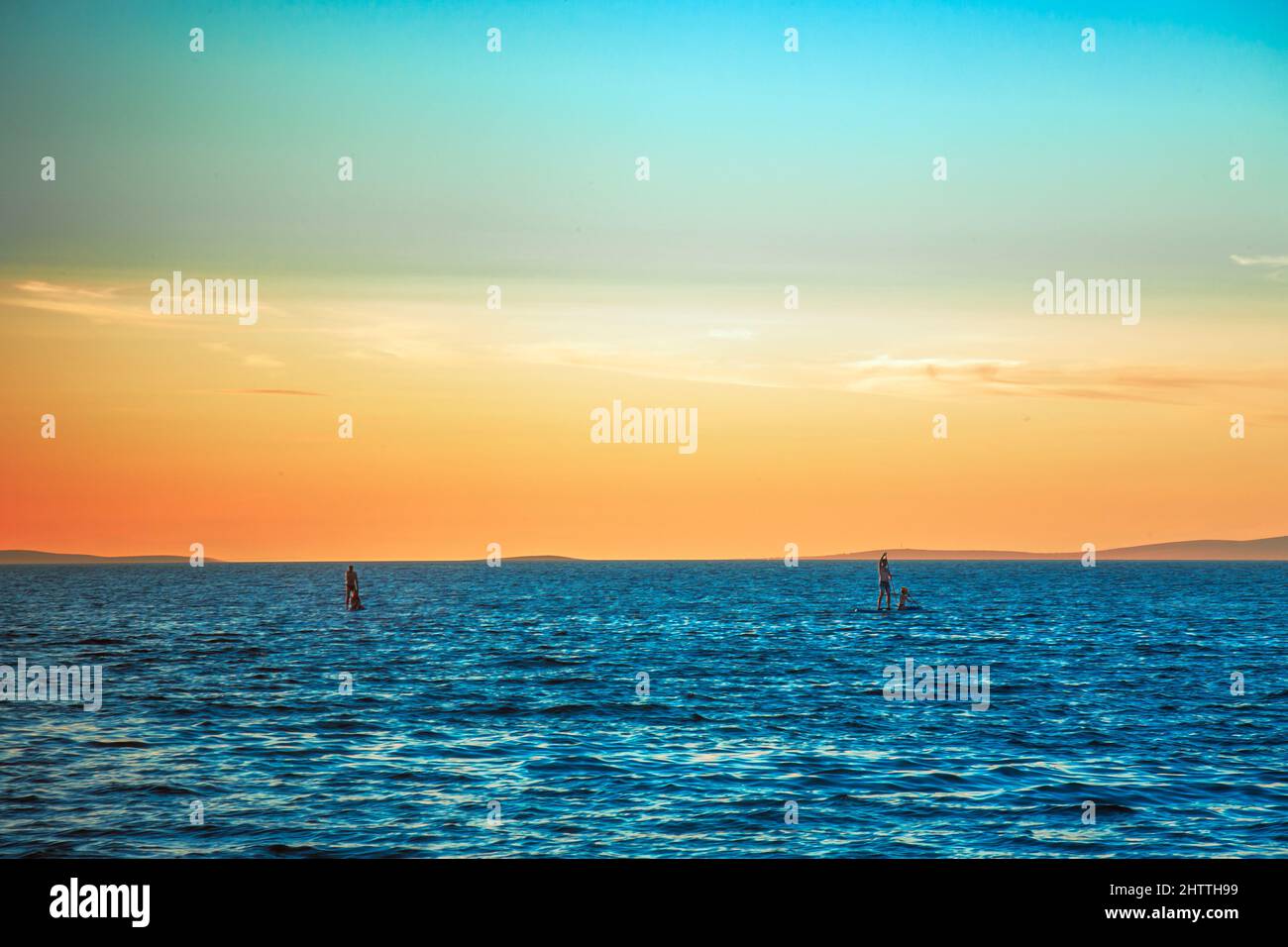 Sunset, blue sea and four people on a two sup boards on the seas. A ...