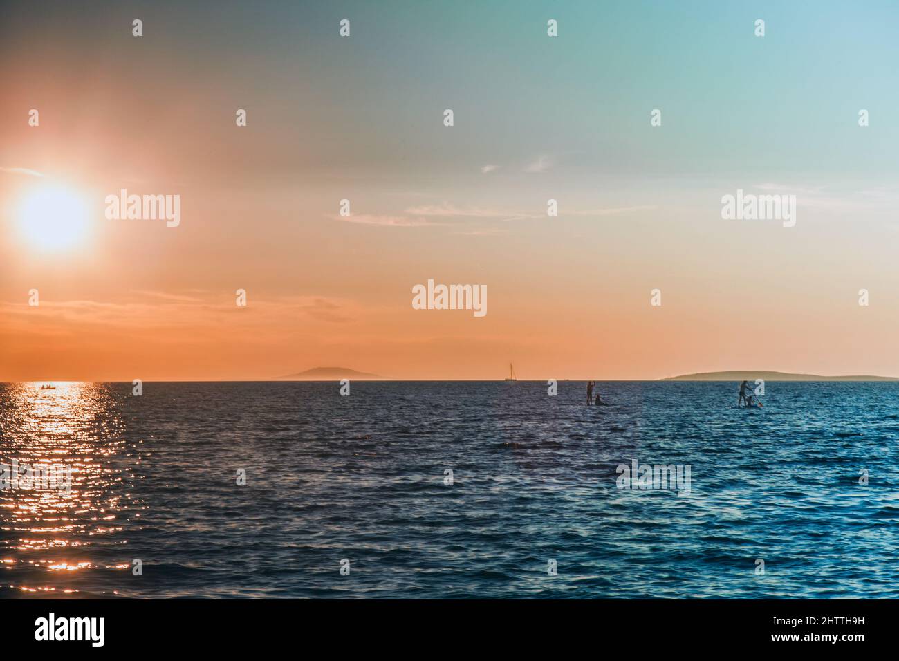 Sunset, blue sea and four people on a two sup boards on the seas. A ...