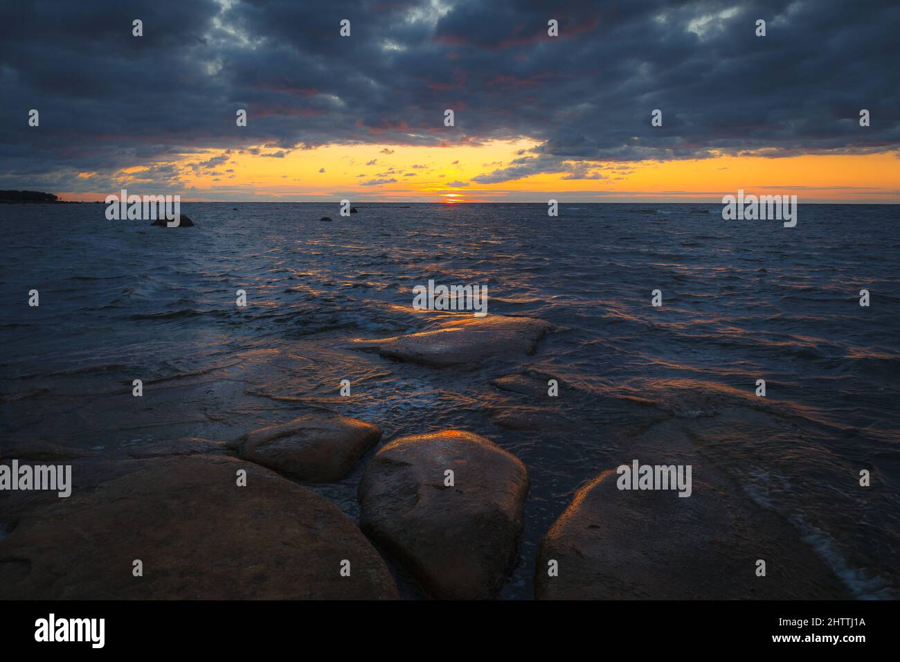 Rocky shore with stones sinking in the sea water. Sunset, long exposure ...