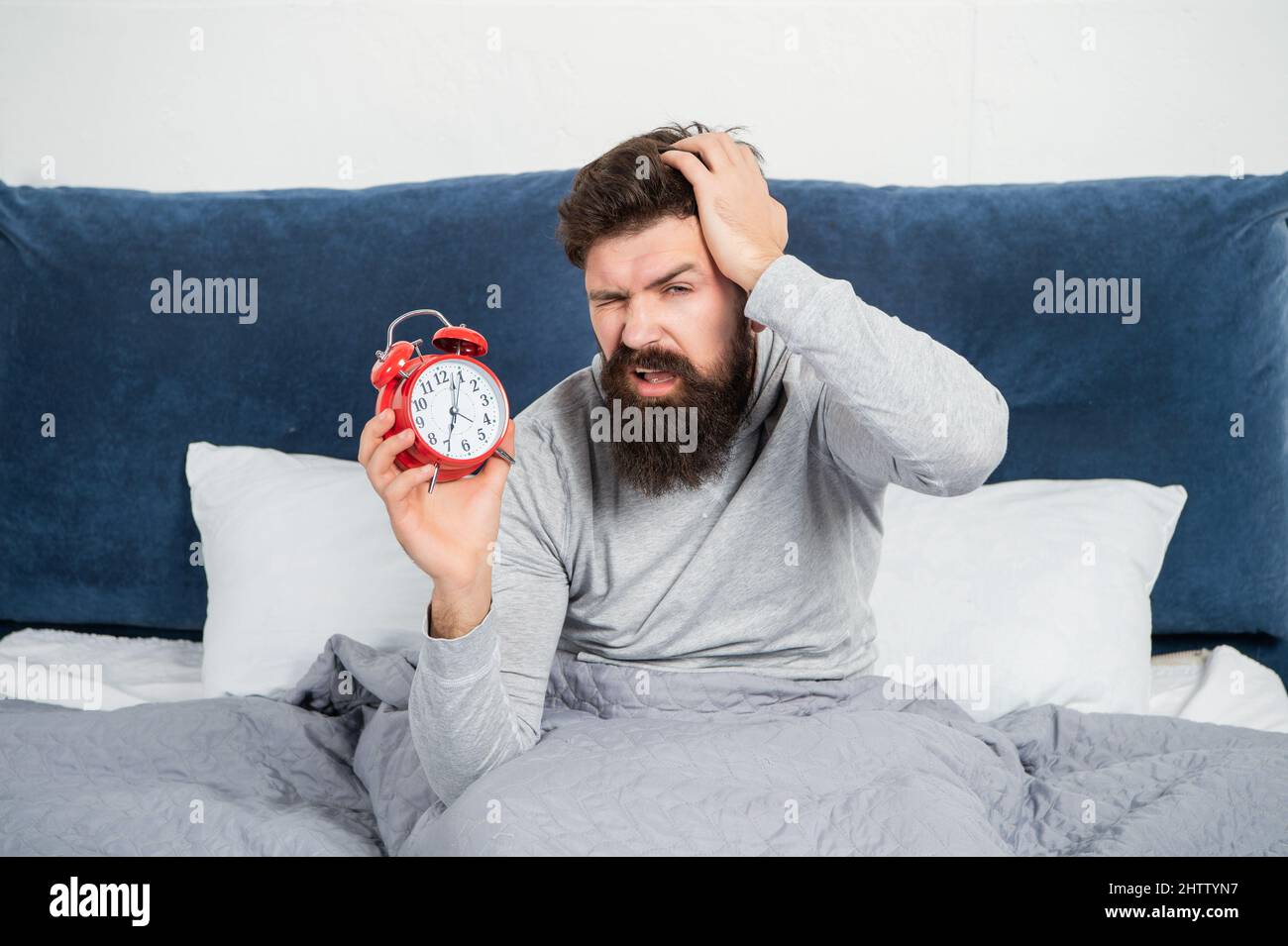 Sleepy guy holding alarm clock being in bed in morning, oversleep Stock ...