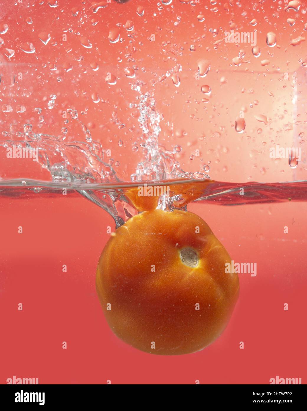 Portrait of a peach fruit dunked in water creates a splash on an orange ...
