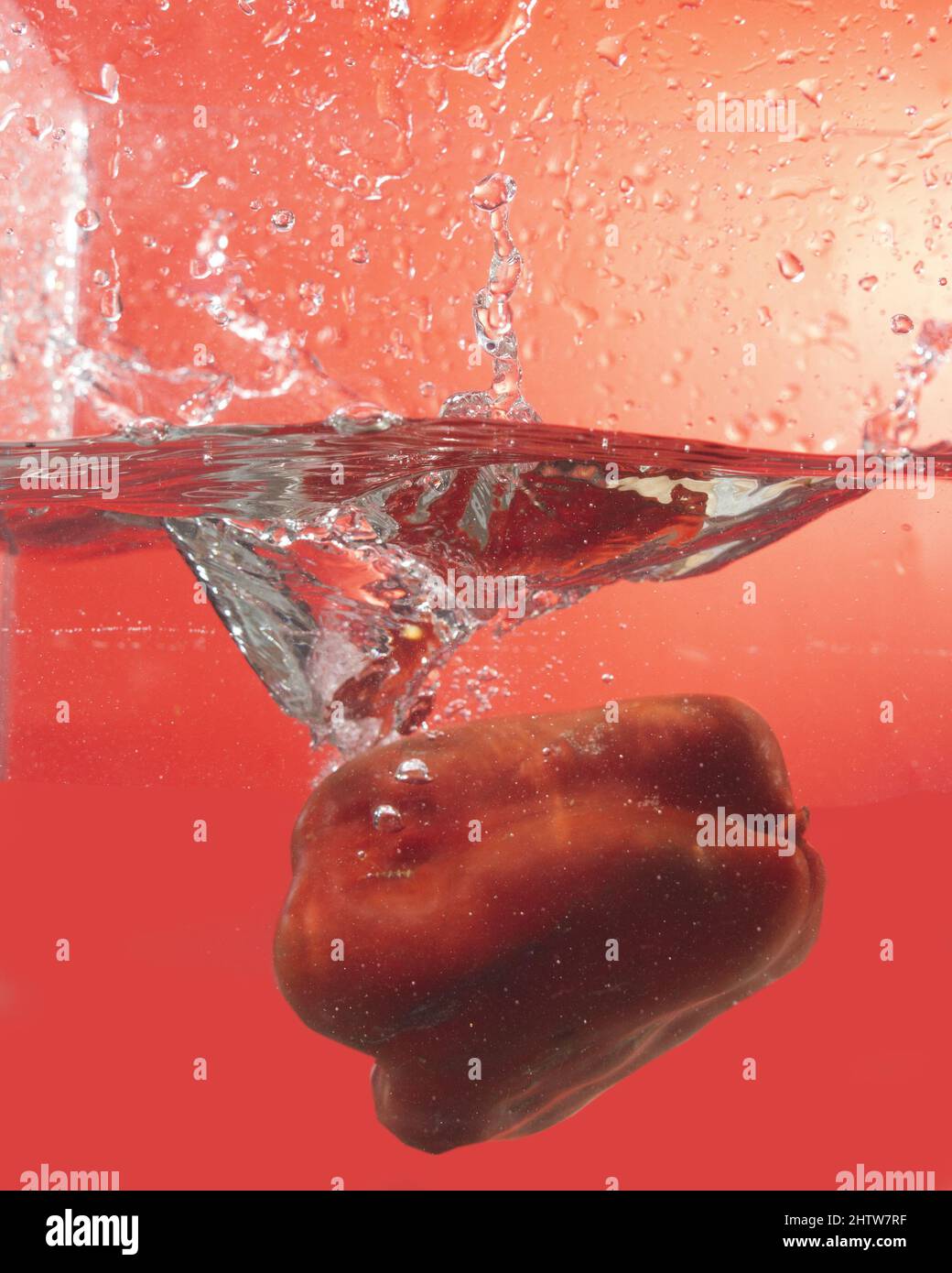 Portrait of capsicum dunked in water creates a splash on an orange ...