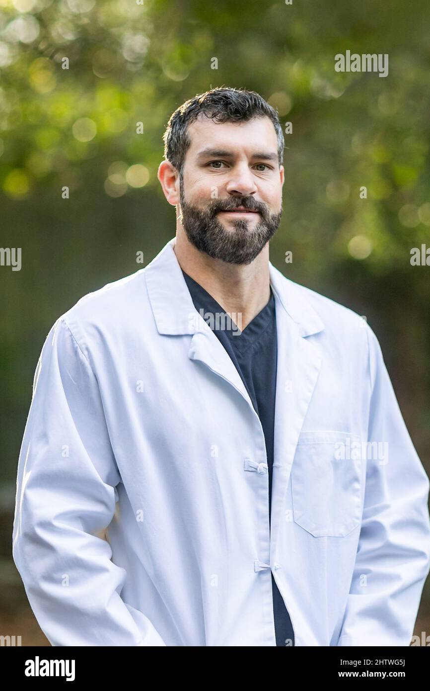 A doctor with dark hair and a beard in a white lab coat standing ...