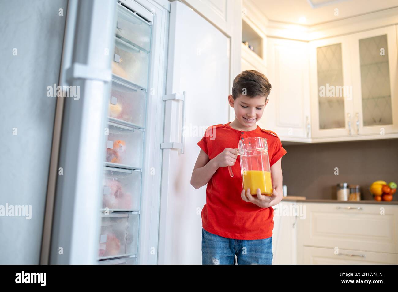 Joyous kid examining orange juice in the jug Stock Photo - Alamy