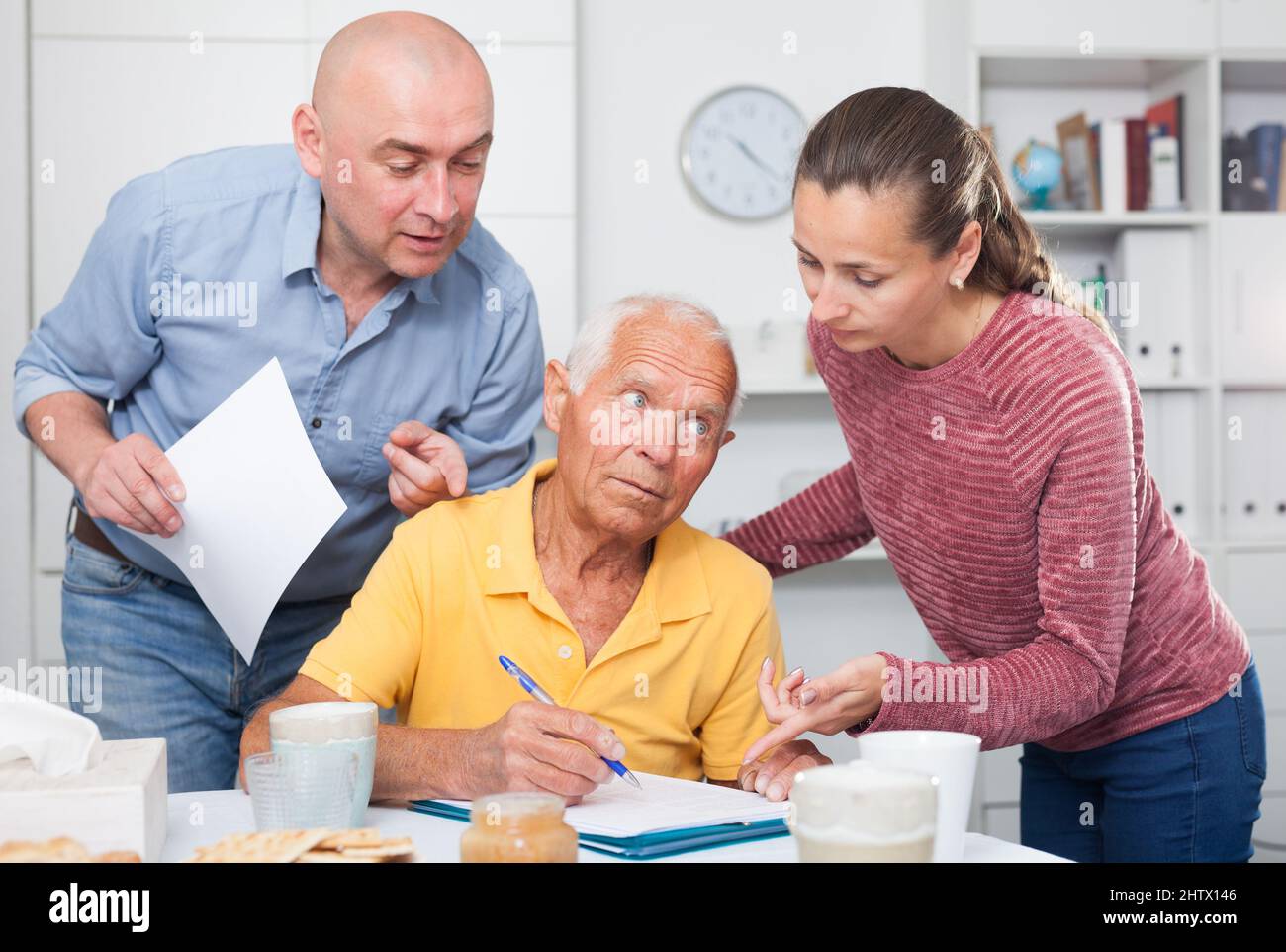 Adult children help an older father sign documents Stock Photo - Alamy