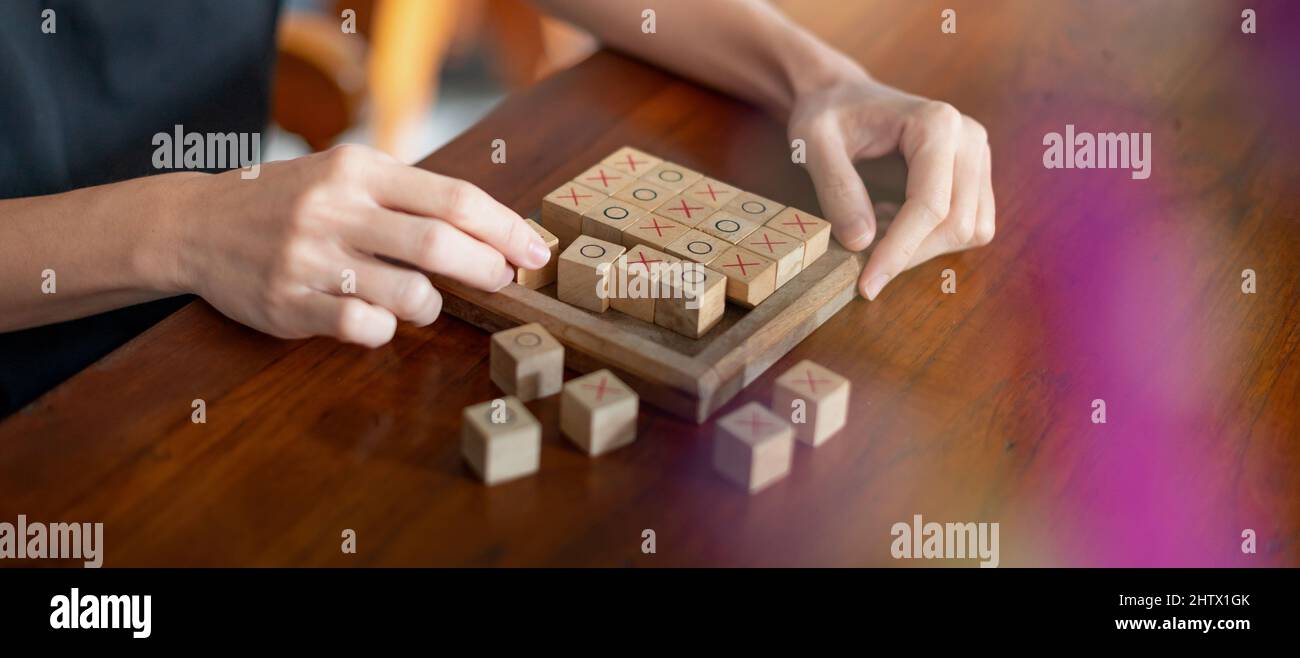 Female hand play tic-tac-toe wood board game XO on a wooden surface ...