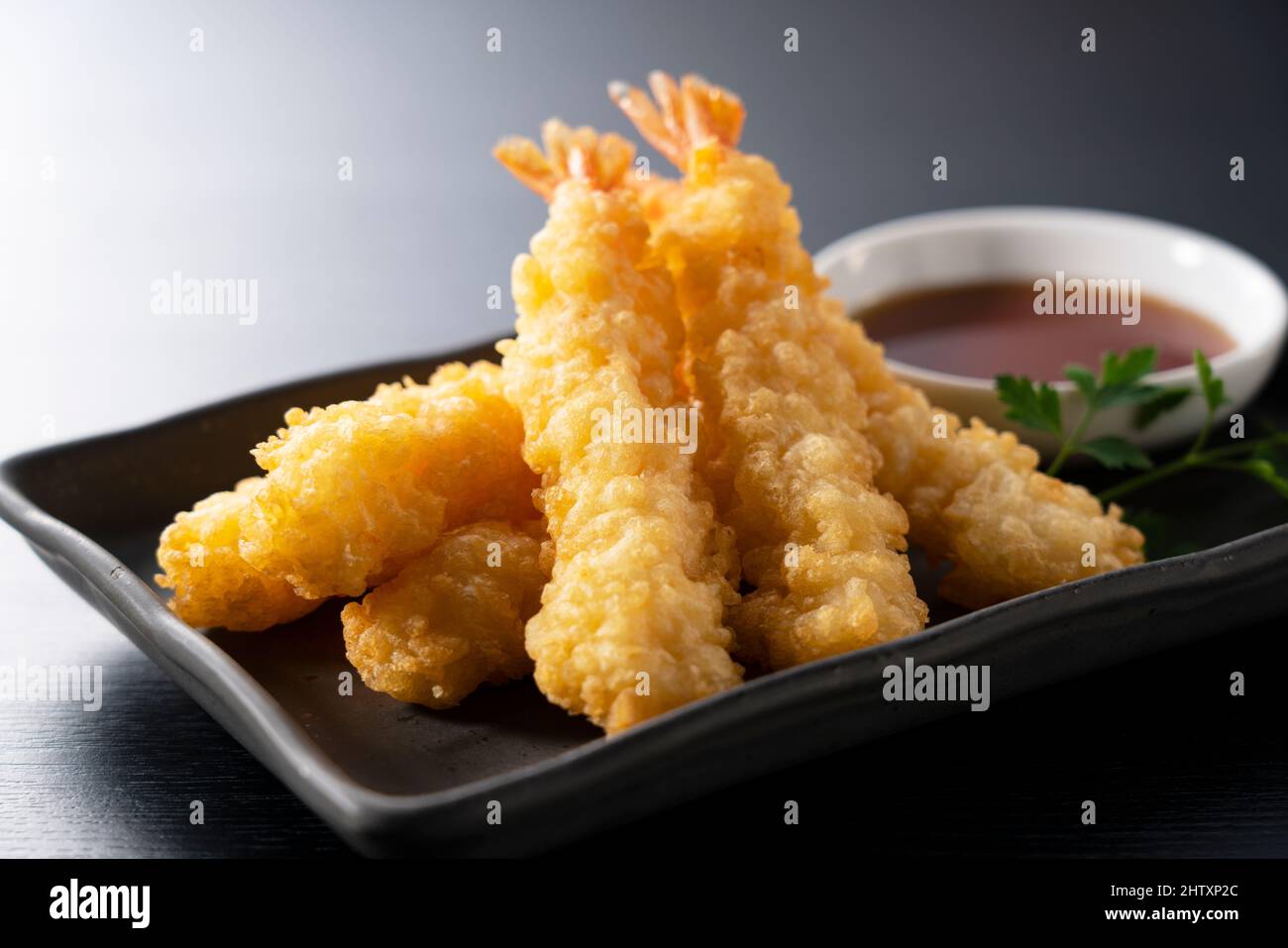 Shrimp tempura on a plate placed against a black background. Tempura is ...