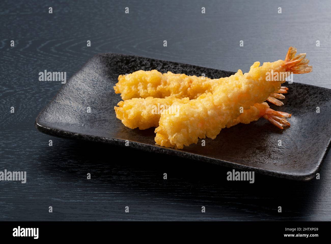 Shrimp tempura on a plate placed against a black background. Tempura is ...