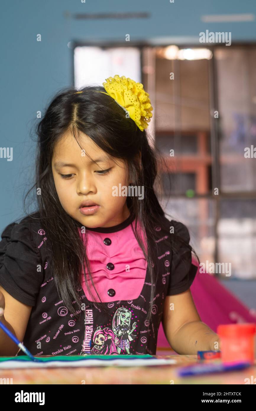 Adorable little Hispanic girl painting with a brush and watercolors ...
