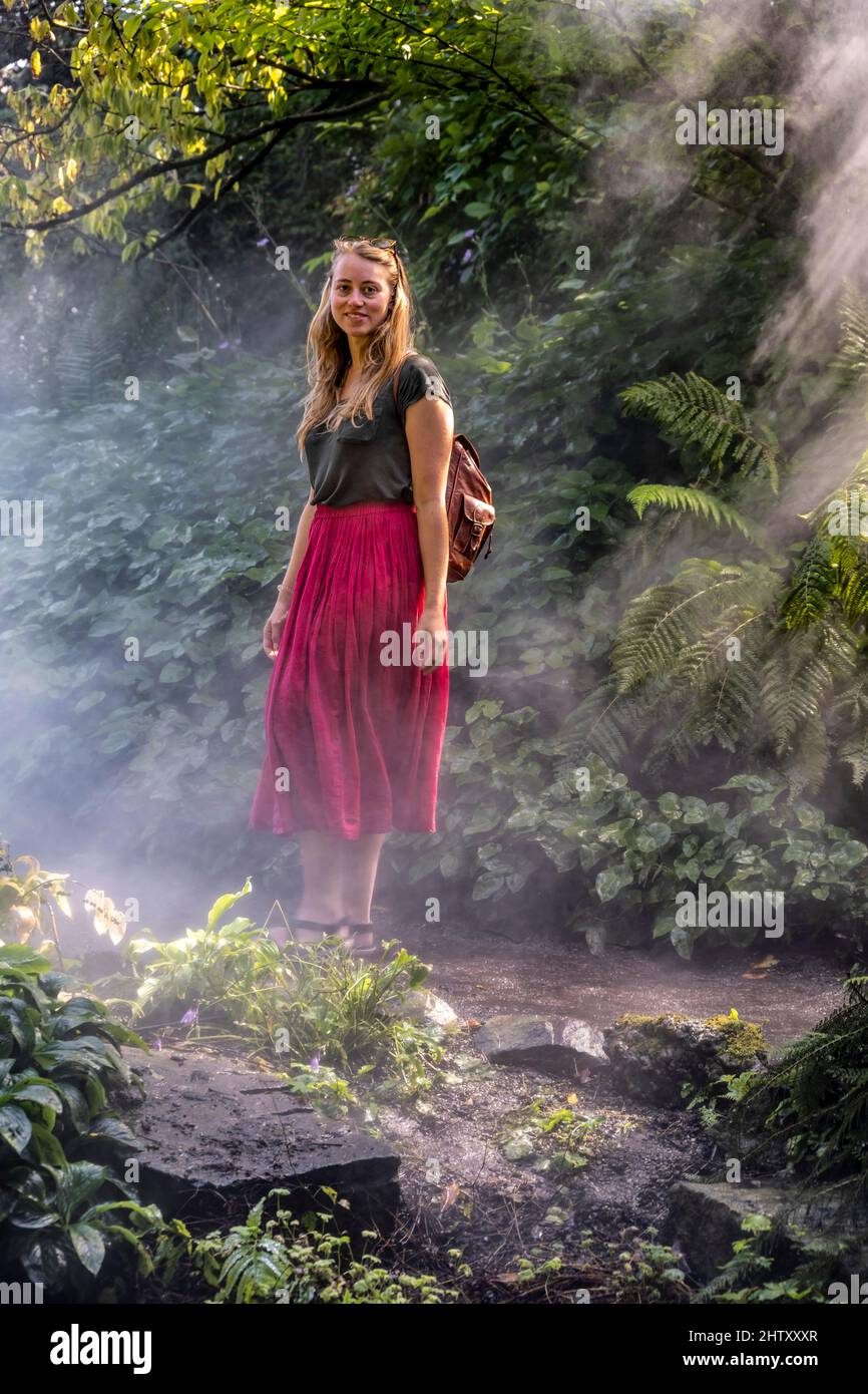 Young woman standing in fog, water vapour in front of dense vegetation ...