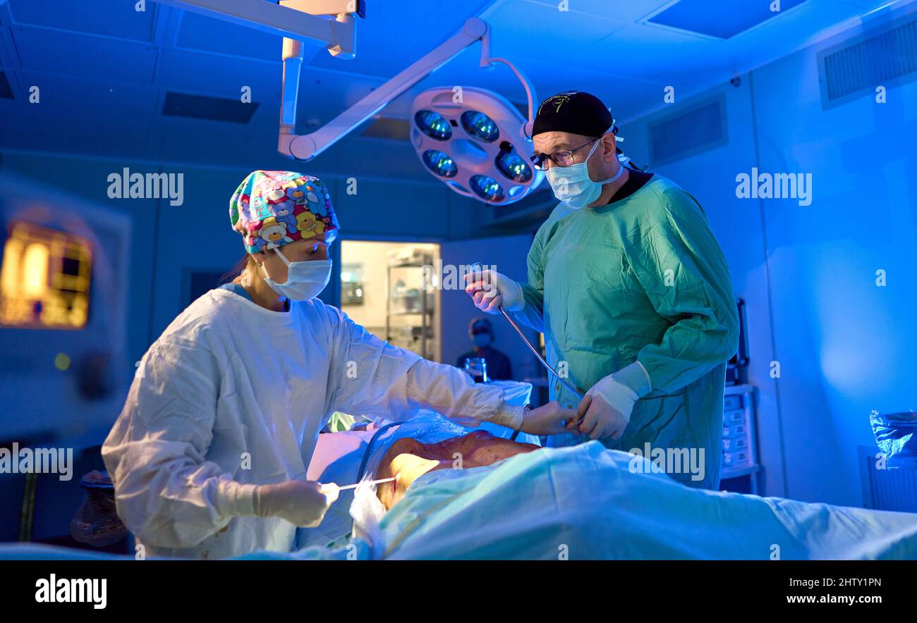 surgeon and an assistant operate on a patient in a blue operating room ...