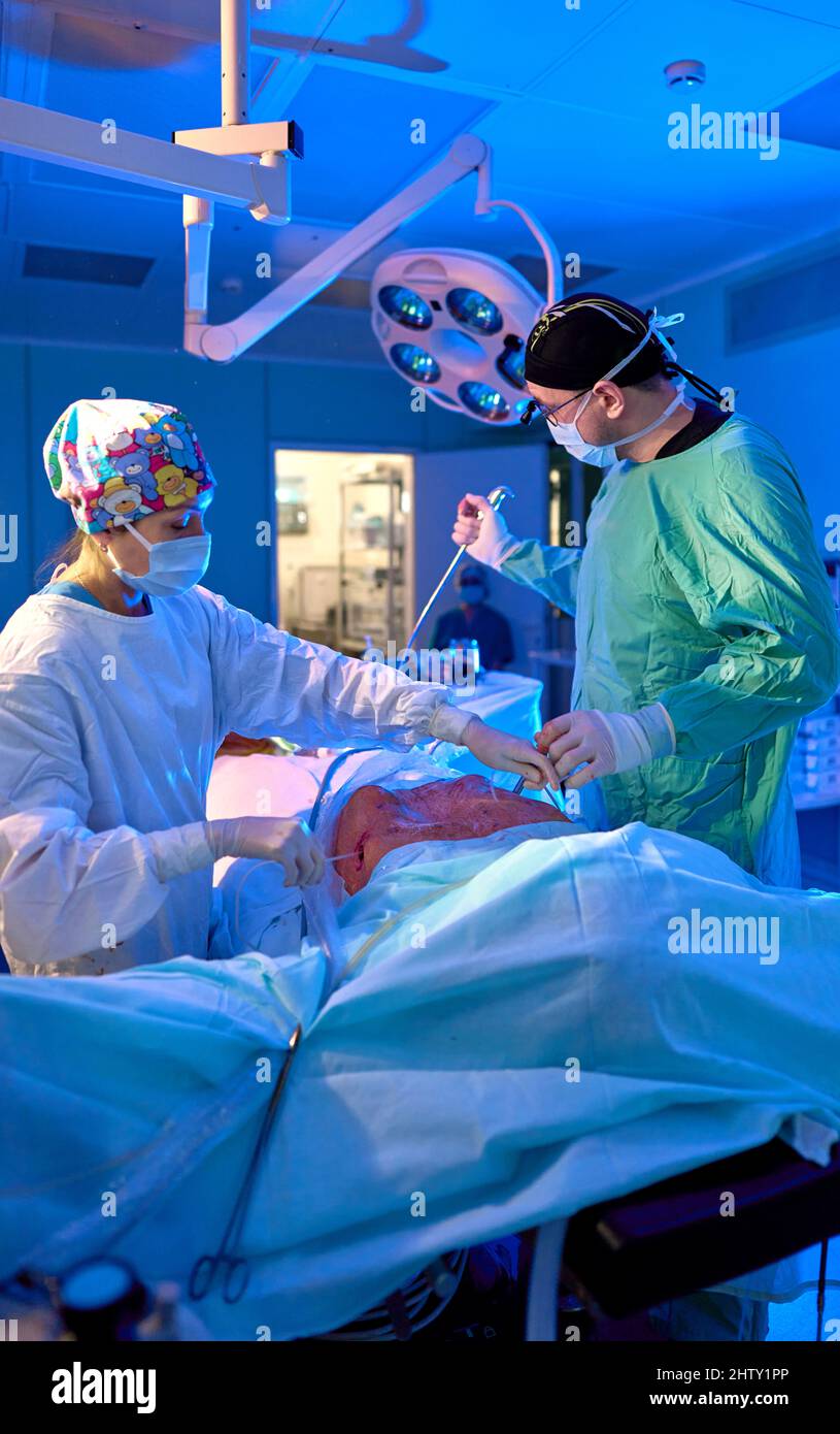 surgeon and an assistant operate on a patient in a blue operating room ...